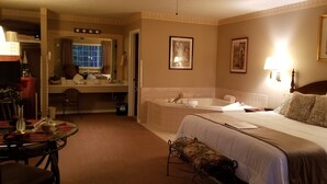 Quarto de hotel com uma cama grande, área de estar com mesa e cadeiras, banheiro com banheira e escrivaninha com cadeira.
