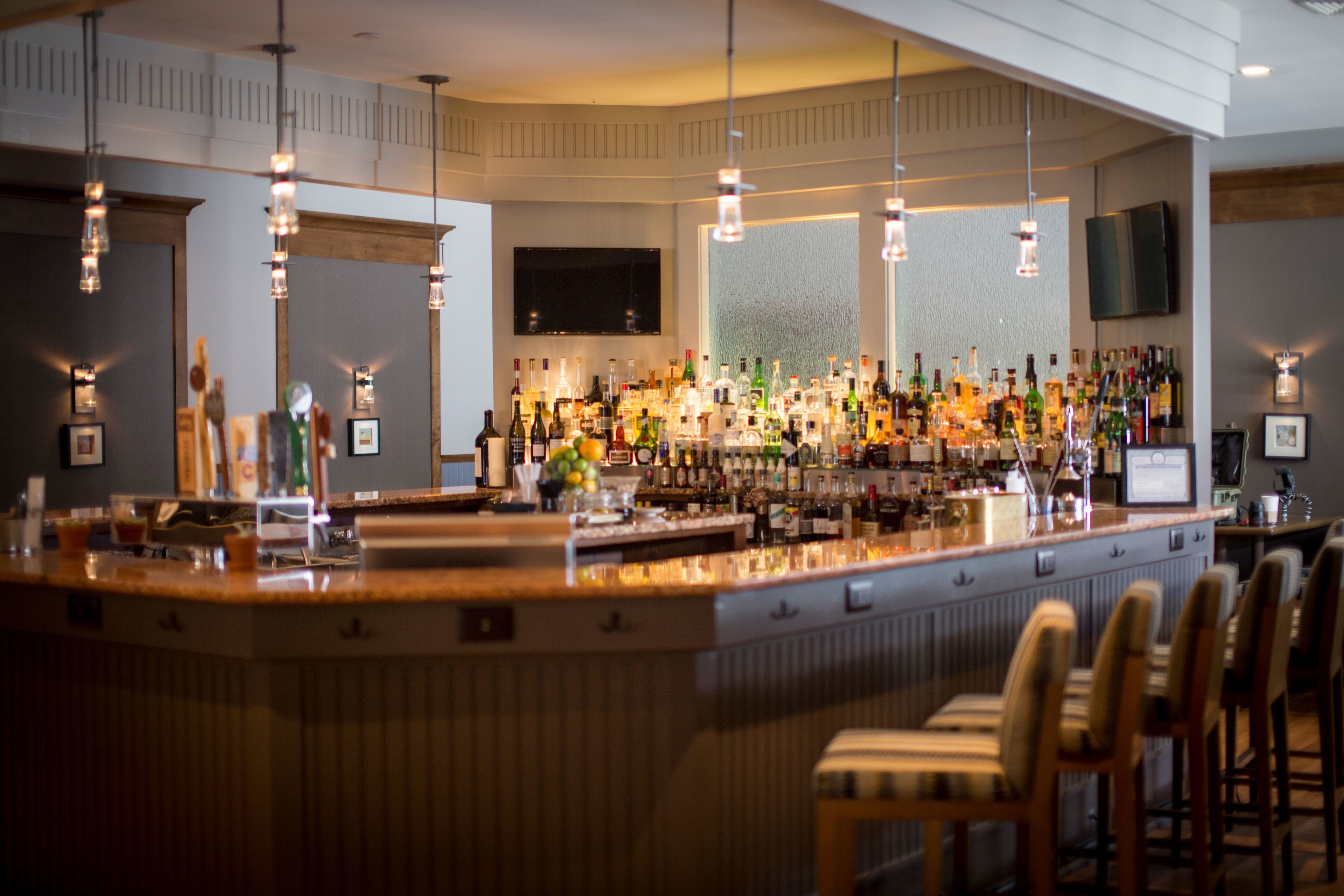 Uma área de bar com balcão, várias luminárias pendentes e uma variedade de garrafas e copos.