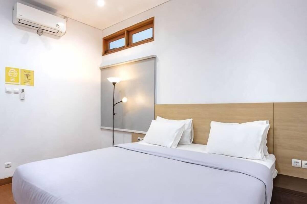 Quarto de hotel com cama, mesa de cabeceira, ar condicionado fixado na parede, janela e luminária na parede.
