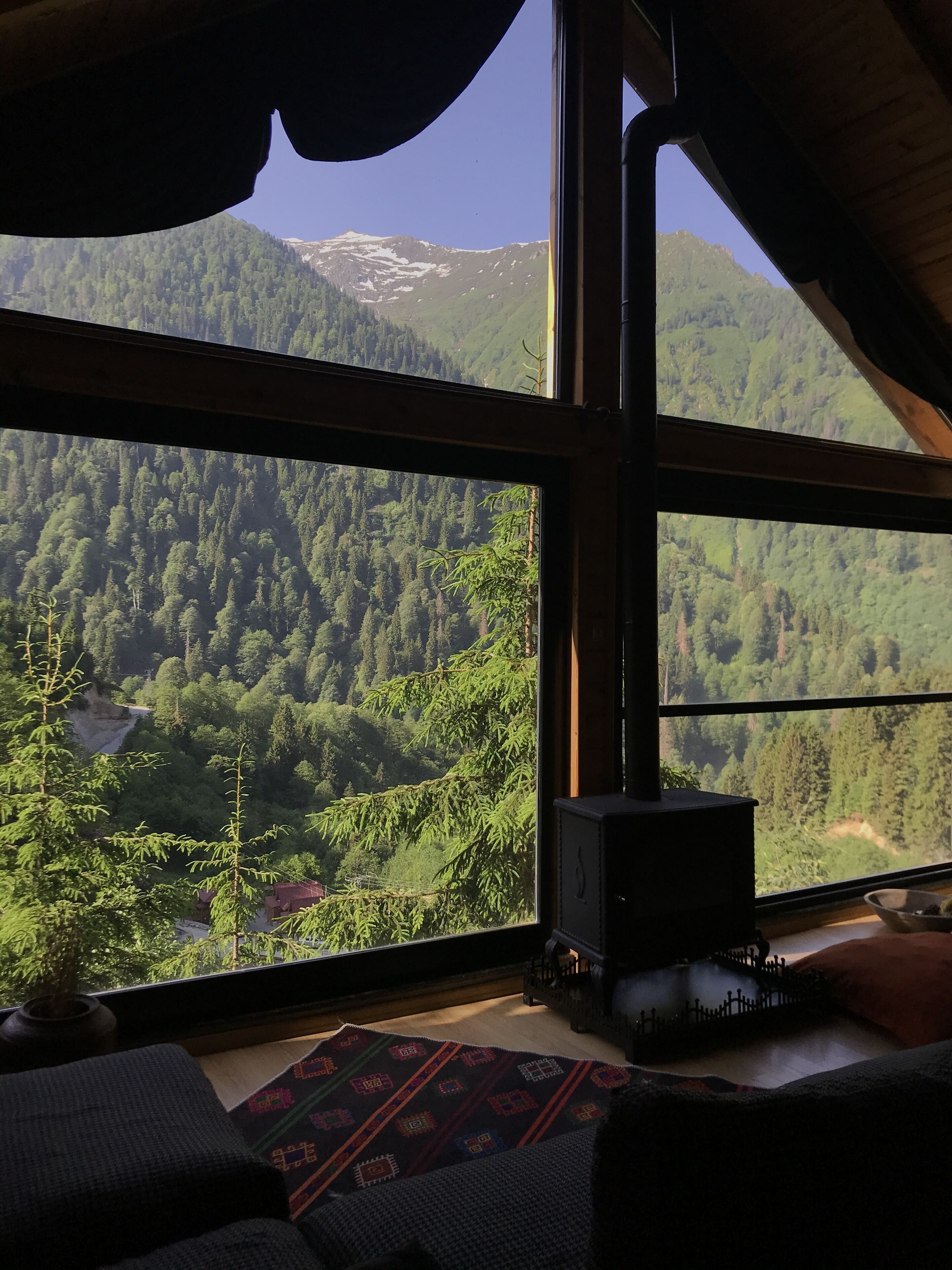 Quarto com uma grande janela que oferece vista para um vale arborizado e montanhas.