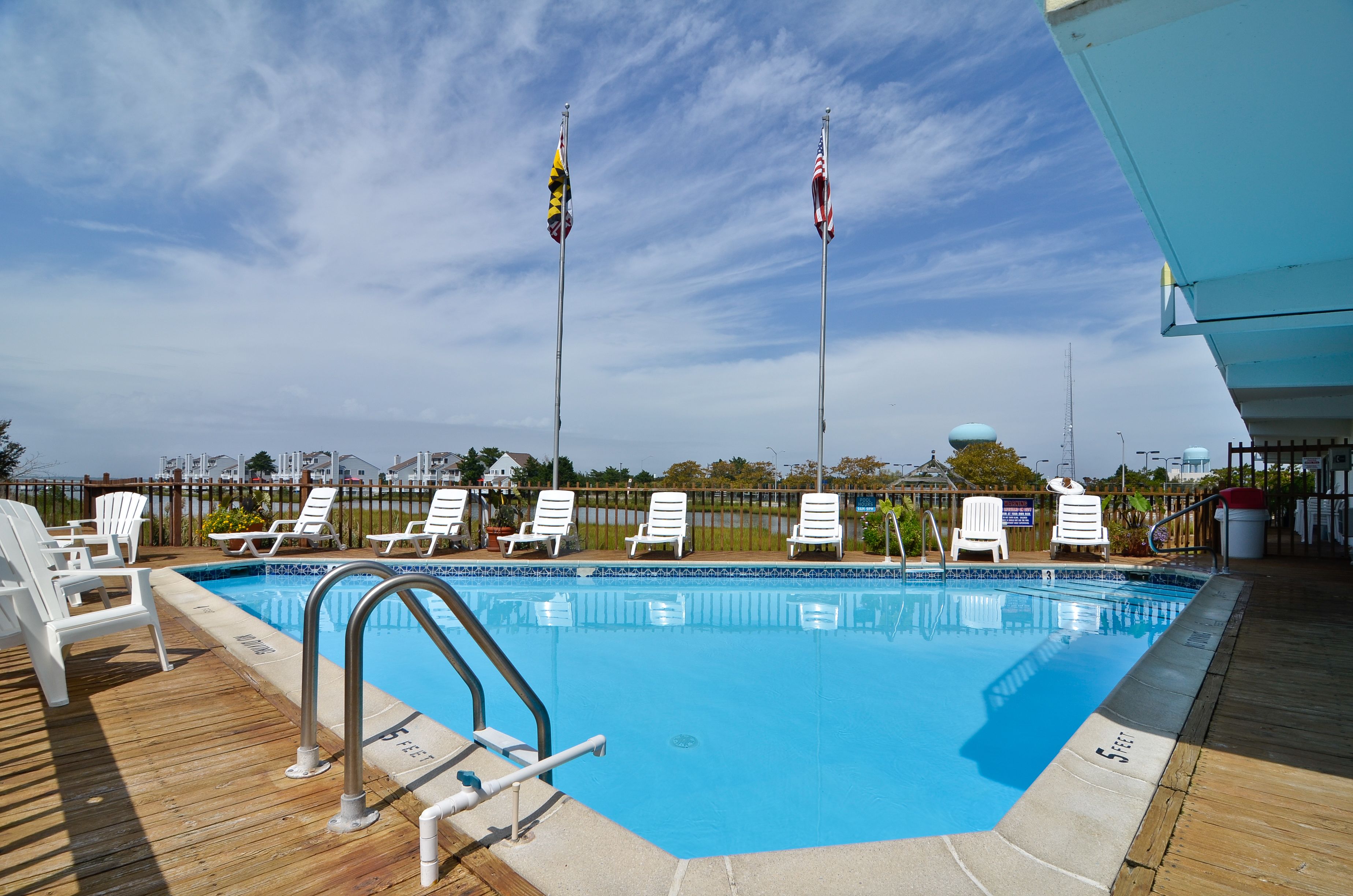 Piscina com espreguiçadeiras e duas bandeiras em mastros.