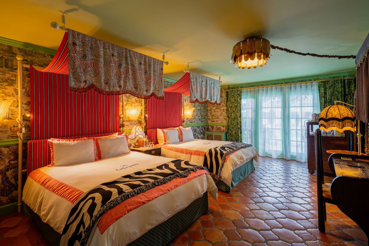 Quarto com duas camas, roupa de cama estampada, soalho de pedra e um candelabro.