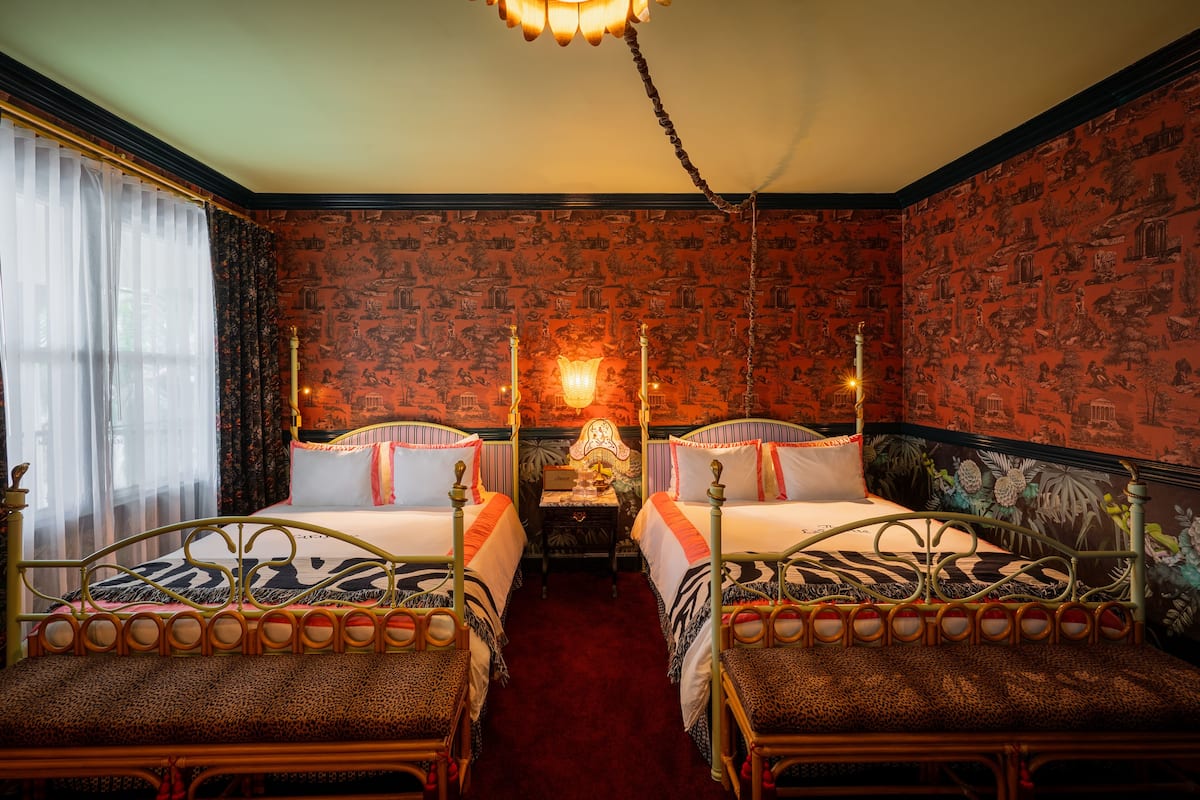 Quarto com duas camas, um candelabro e papel de parede estampado.