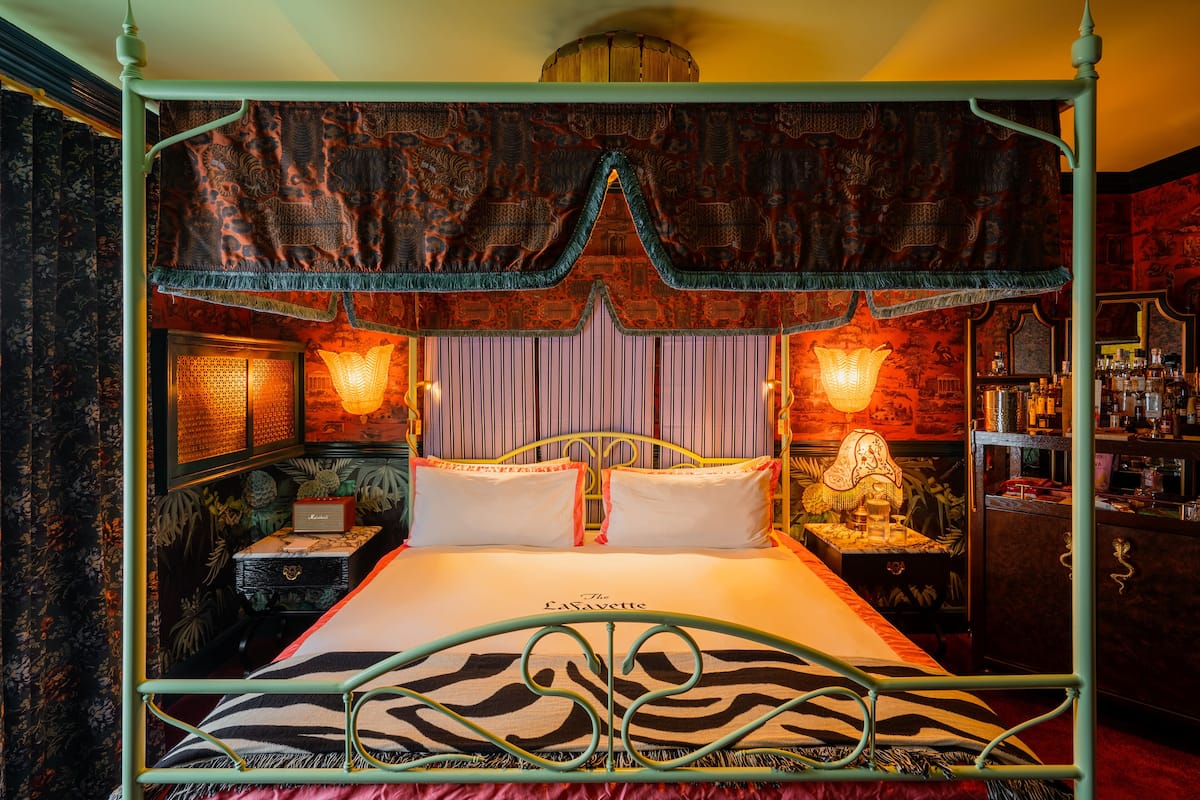 Uma cama de dossel com colcha de estampa de zebra, uma mesinha de cabeceira com abajur e uma cabeceira decorativa.