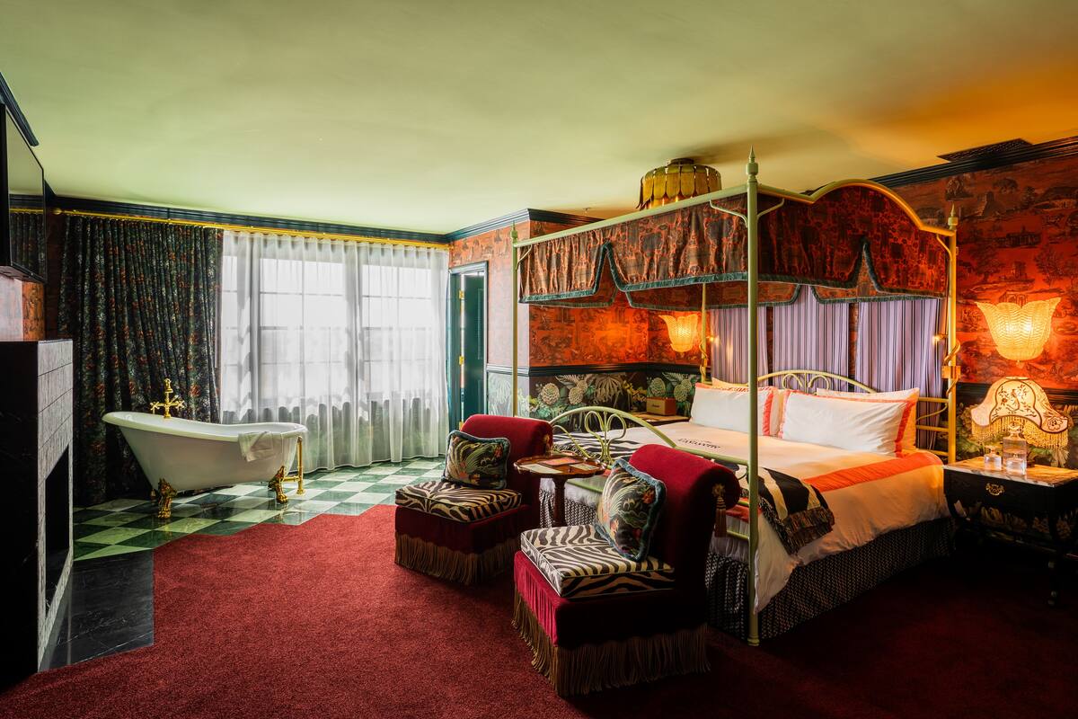 Quarto com cama de dossel, banheira de patas de leão, duas poltronas e uma mesinha.