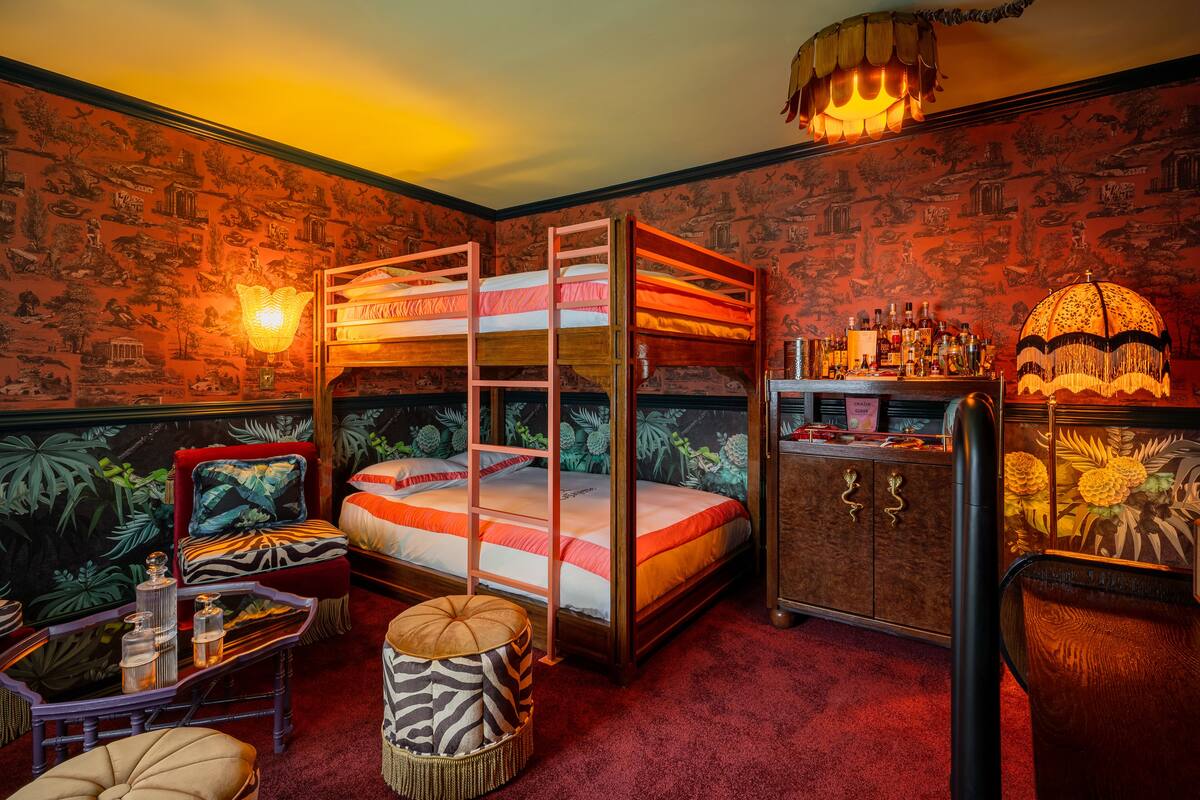 Quarto com beliche, uma mesinha com garrafas, luminária e armário.