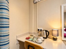 Quarto de hotel com cozinha compacta, chaleira, bandeja com alimentos e luminária.