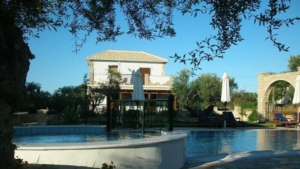 Área de piscina com uma fonte, espreguiçadeiras e um edifício ao fundo.