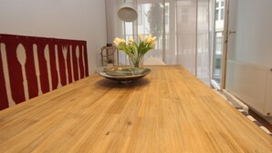 Uma mesa de jantar de madeira com uma tigela de vidro e flores, uma parede com padrão vermelho, e uma janela com vista.