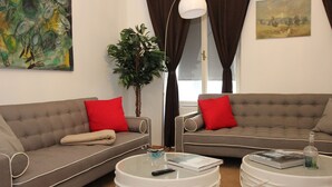 Sala de estar com dois sofás cinzas, almofadas vermelhas, uma mesa de centro de vidro, uma planta e obras de arte nas paredes.