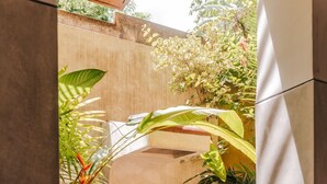 Área de chuveiro com piso de pedra, rodeada por vegetação exuberante e uma parede bege.