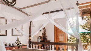 Quarto com cama de dossel, cabeceira de madeira e mesa de cabeceira com objetos decorativos.