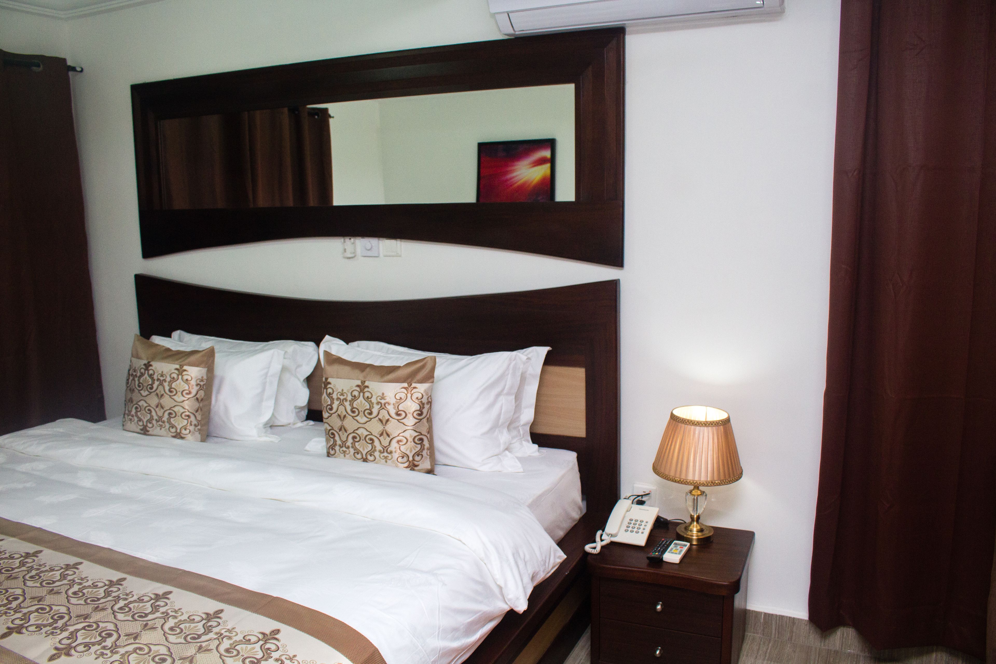 Quarto de hotel com uma cama grande, telefone ao lado da cama e mesa de cabeceira com abajur.