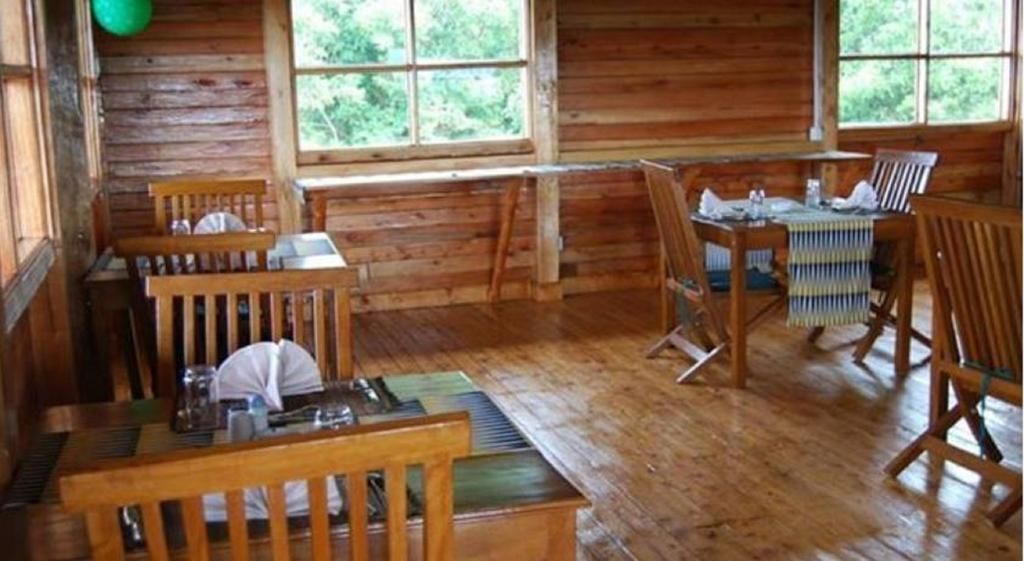 Uma cabana de madeira com área de jantar, incluindo mesa e cadeiras, janelas amplas e vista para o verde lá fora.