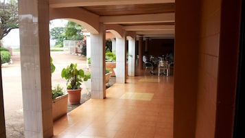 Área externa coberta com piso de azulejos, plantas em vasos e um espaço de estar com cadeiras e mesas.