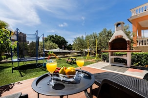 Um pátio externo com uma mesa posta para o café da manhã, um trampolim e um forno de tijolos.