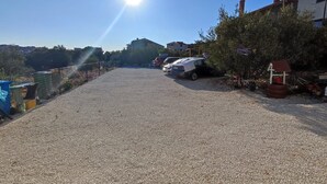 Um espaço de estacionamento com paralelepípedos, com dois carros estacionados, rodeado por edifícios e árvores.