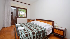 Quarto com cama, mesa de cabeceira, janela com cortinas e vista para o exterior.