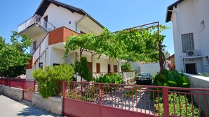 Um prédio residencial com varanda, entrada por portão e um carro estacionado.