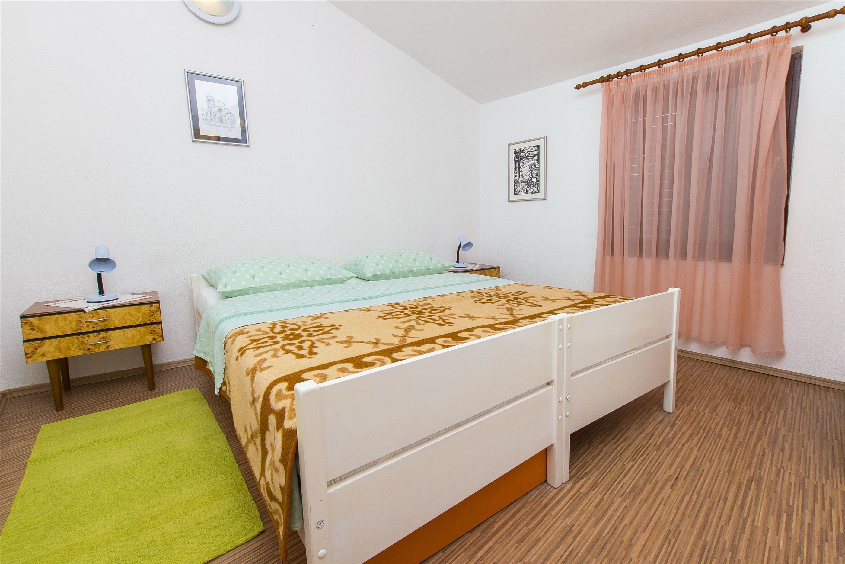 Quarto com cama, mesa de cabeceira, abajur, quadro na parede e janela com cortinas.