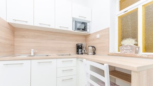 Cozinha com armários brancos, micro-ondas, cafeteira e janela com um objeto decorativo.