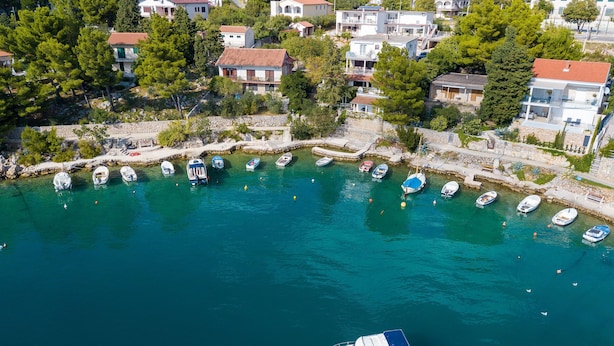 Uma vila costeira com casas, um muro de pedra e barcos atracados na orla.