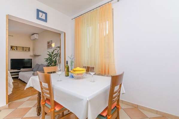 Uma sala de jantar com uma mesa posta para dois, uma televisão ao fundo e uma planta sobre a mesa.