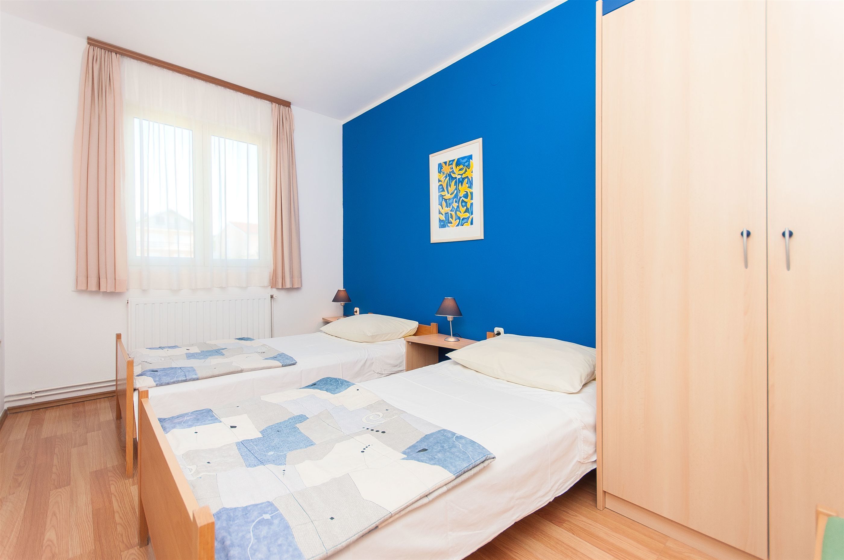 Quarto com duas camas, parede azul e guarda-roupa de madeira.