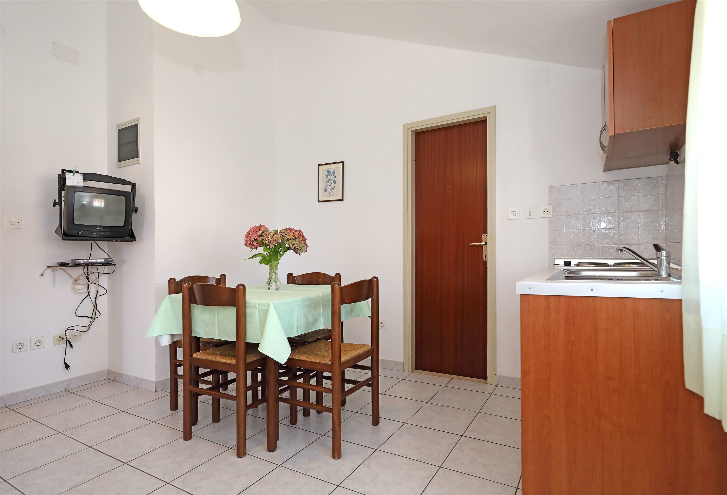 Uma cozinha compacta com mesa, cadeiras, uma televisão pequena e uma porta.