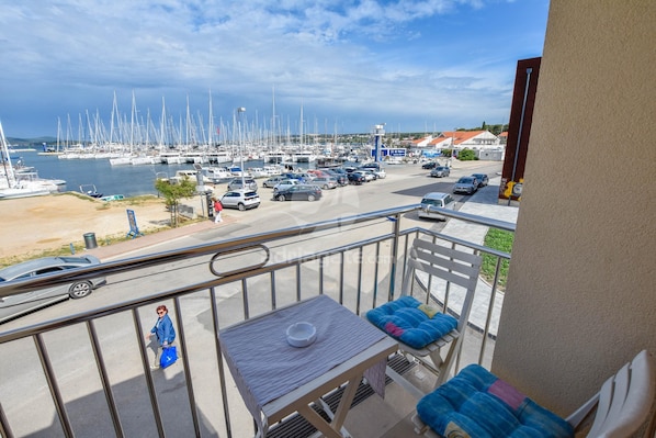 Varanda com mesa e cadeiras, com vista para uma marina com barcos e carros.