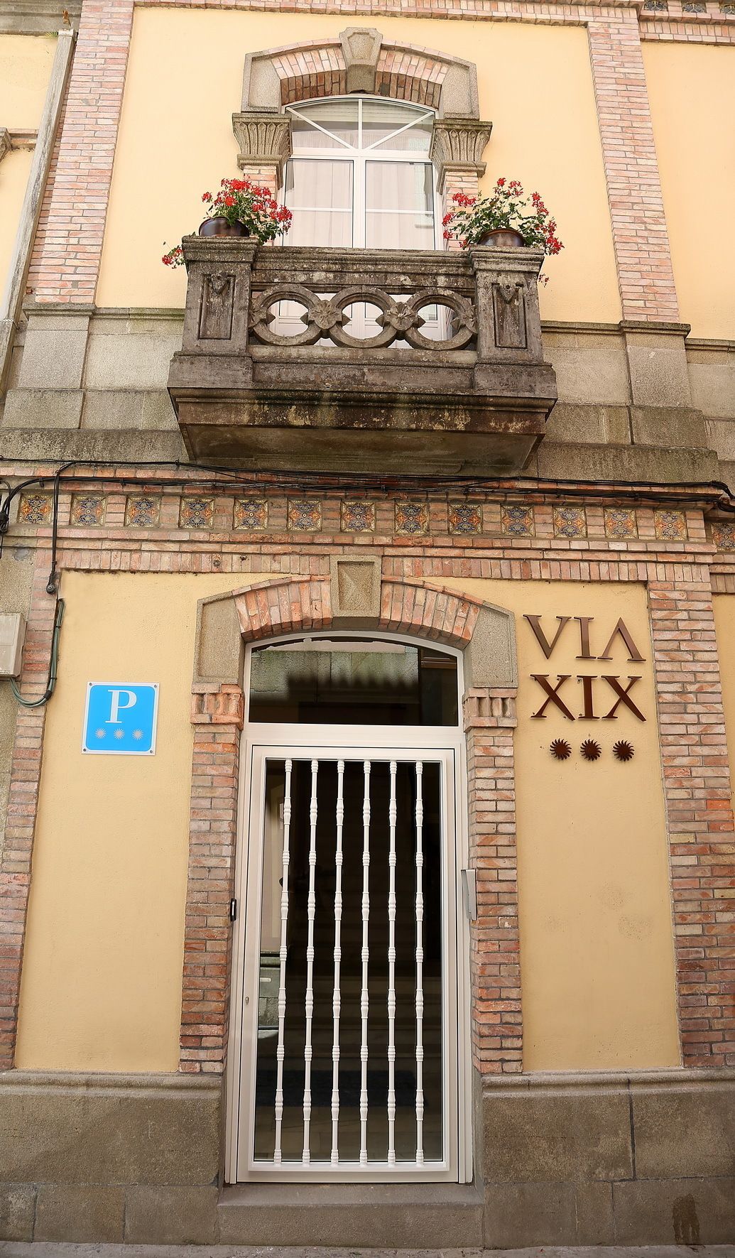 Fachada de edifício com parede amarela, porta branca com barras verticais e varanda florida.