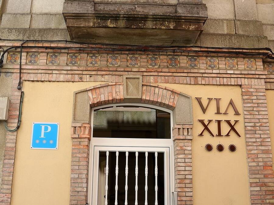 Fachada de edifício com parede amarela, porta branca com barras verticais e varanda florida.