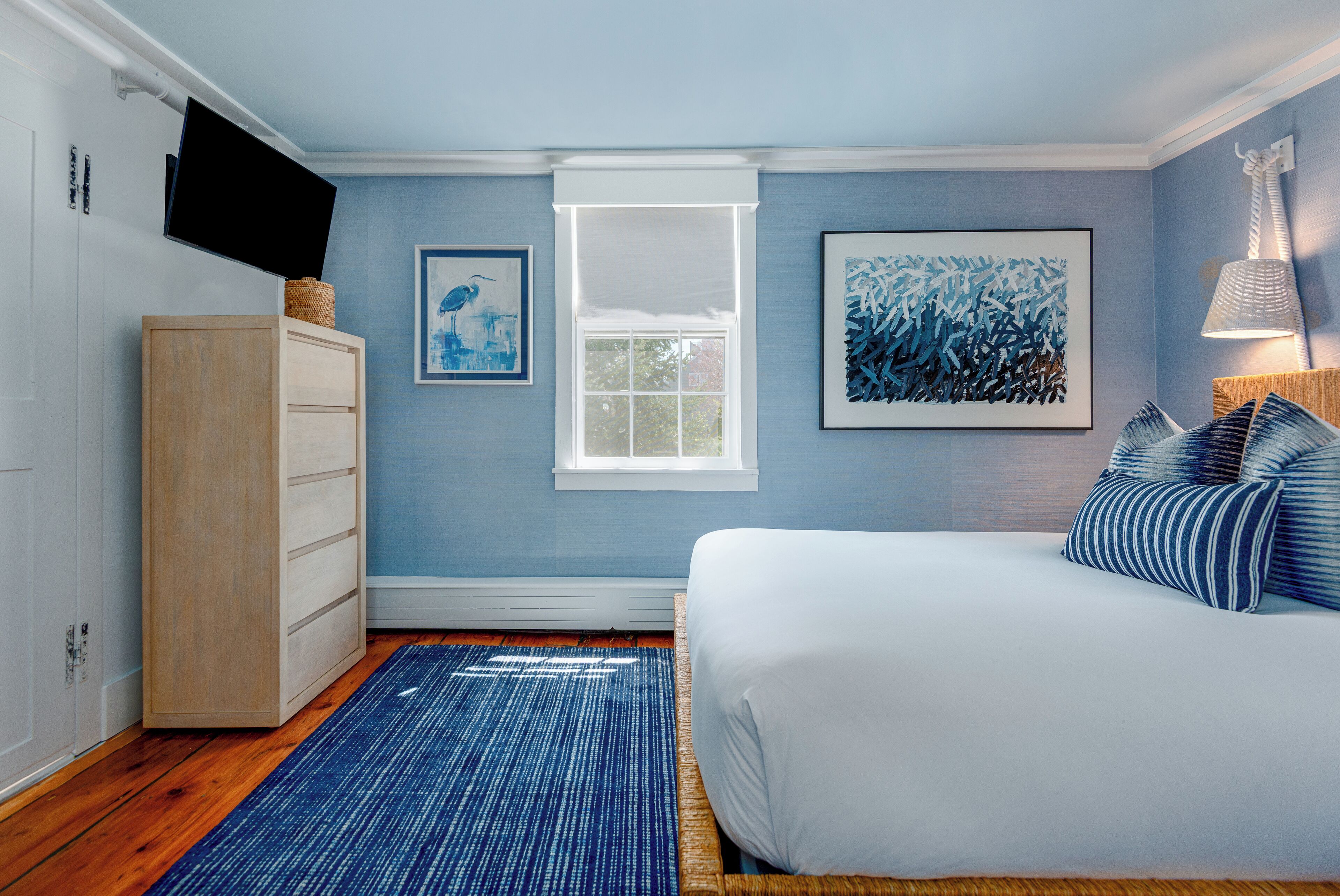 Quarto com cama, penteadeira, janela e obras de arte nas paredes.