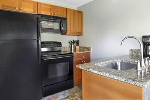 Cozinha equipada com geladeira preta, micro-ondas, forno, armários de madeira, bancada de granito e pia de aço inoxidável.