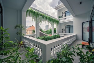 Uma varanda com guarda-corpo branco, plantas verdes e vista para um edifício com telhado vermelho.