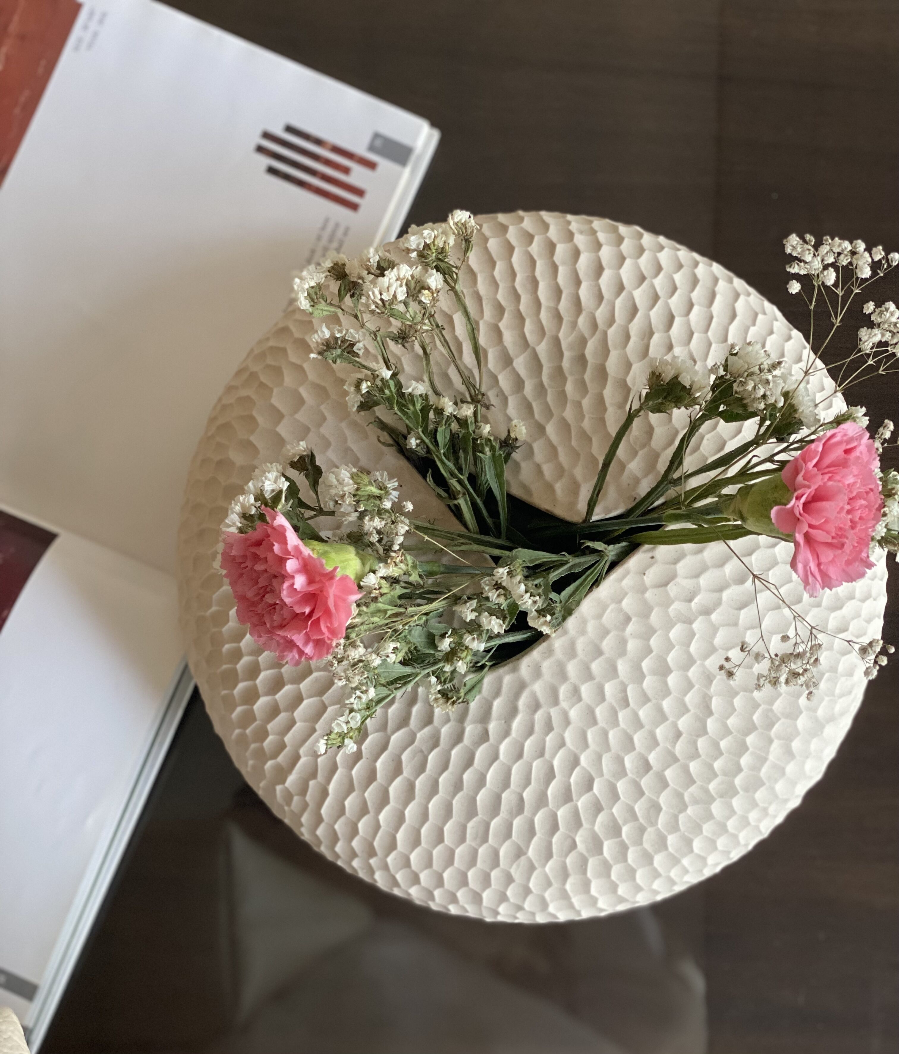 Uma mesa branca e arredondada com textura, adornada com um arranjo de flores.