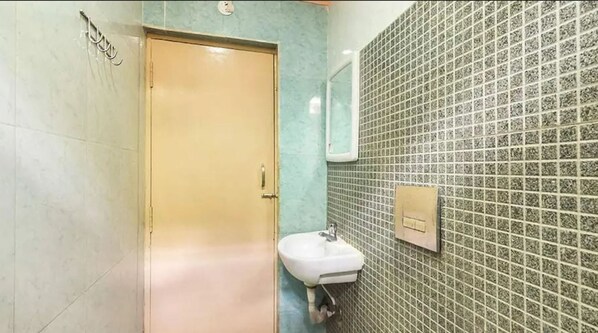 Casa de banho com porta bege, pia branca e parede revestida com padrão de grelha.