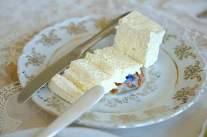 Um prato com um design branco e dourado, contendo um pedaço de alimento branco, possivelmente tofu, e uma faca.