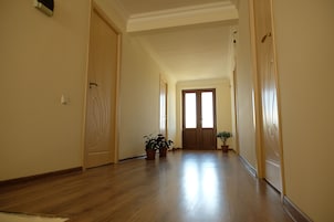 Um corredor com piso de madeira, paredes em tom bege e uma porta no fim.