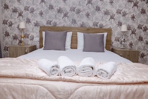 Cama bem arrumada com cabeceira, duas mesas de cabeceira com abajures e papel de parede floral.