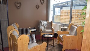 Um quarto aconchegante com móveis de madeira, uma mesa pequena com peças de xadrez e uma vista pela janela.