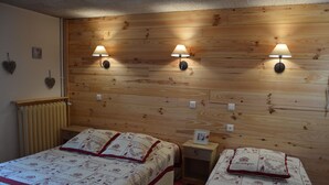 Quarto com duas camas, paredes de painel de madeira e duas luminárias fixadas na parede.