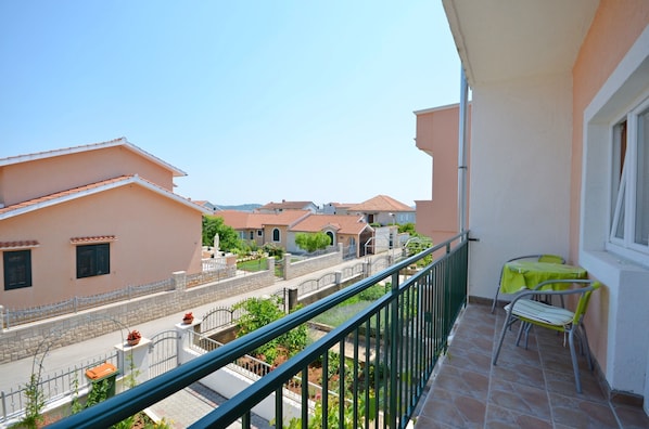 Uma varanda com vista para uma rua residencial, um pequeno jardim e uma mesa com cadeiras.