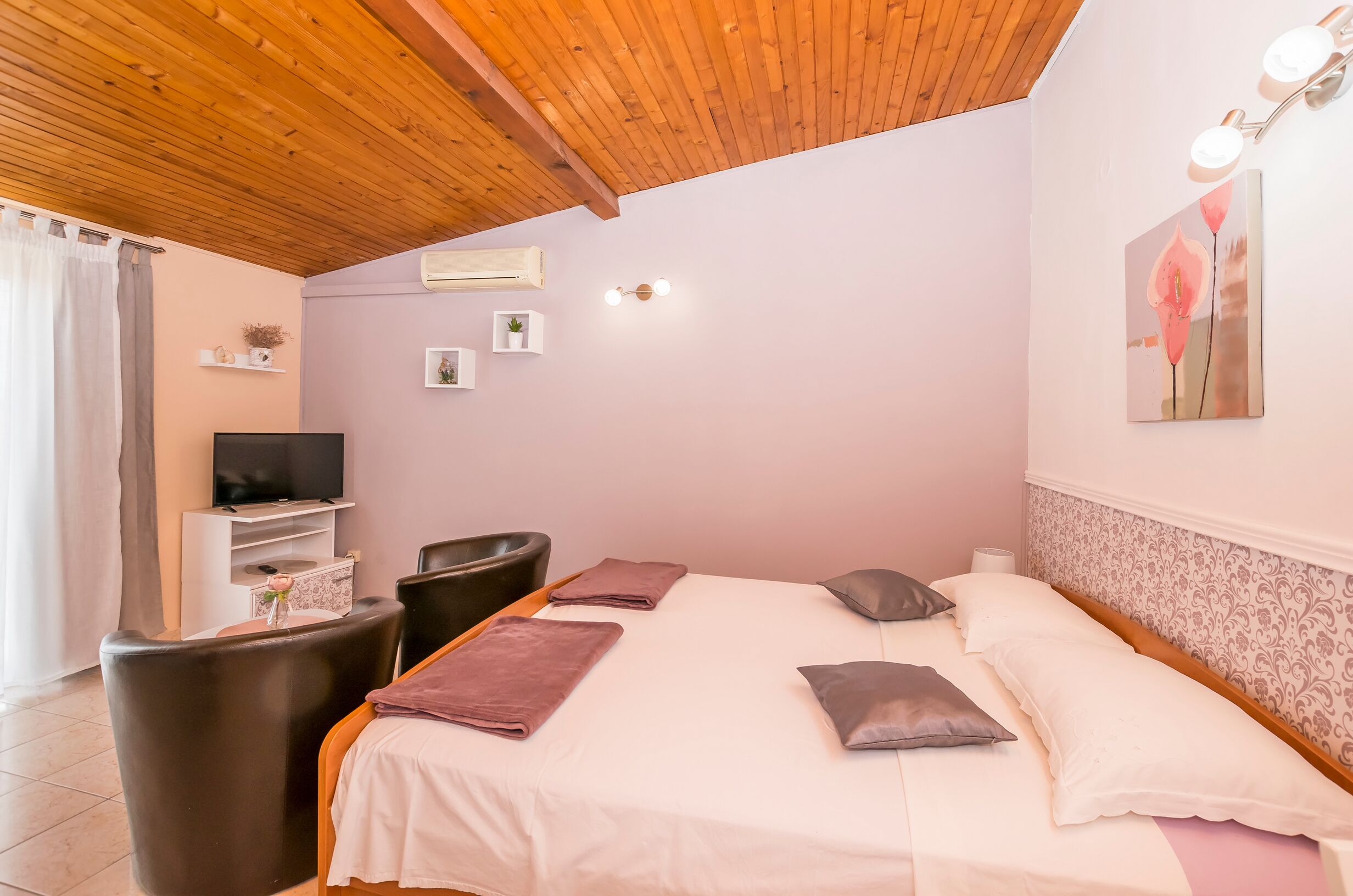 Quarto com cama, televisão, cadeira e teto com vigas de madeira.