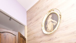 Um quarto com porta de madeira, uma mesa redonda com um vaso e xícaras de chá, e um quadro pendurado na parede.