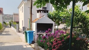 Rua residencial com casas, churrasqueira e plantas floridas.