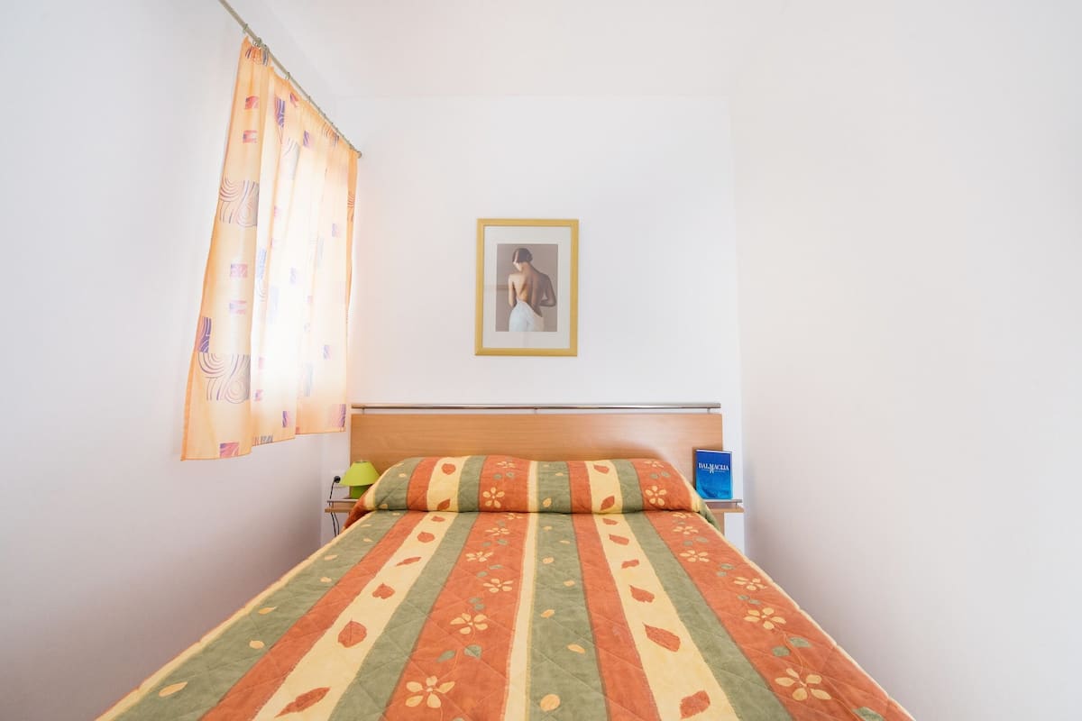 Uma cama bem arrumada com colcha listrada, um quadro na parede e uma cortina na janela.