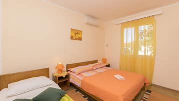 Quarto de hotel com duas camas, uma janela com cortinas amarelas, ar condicionado e um pequeno quadro na parede.
