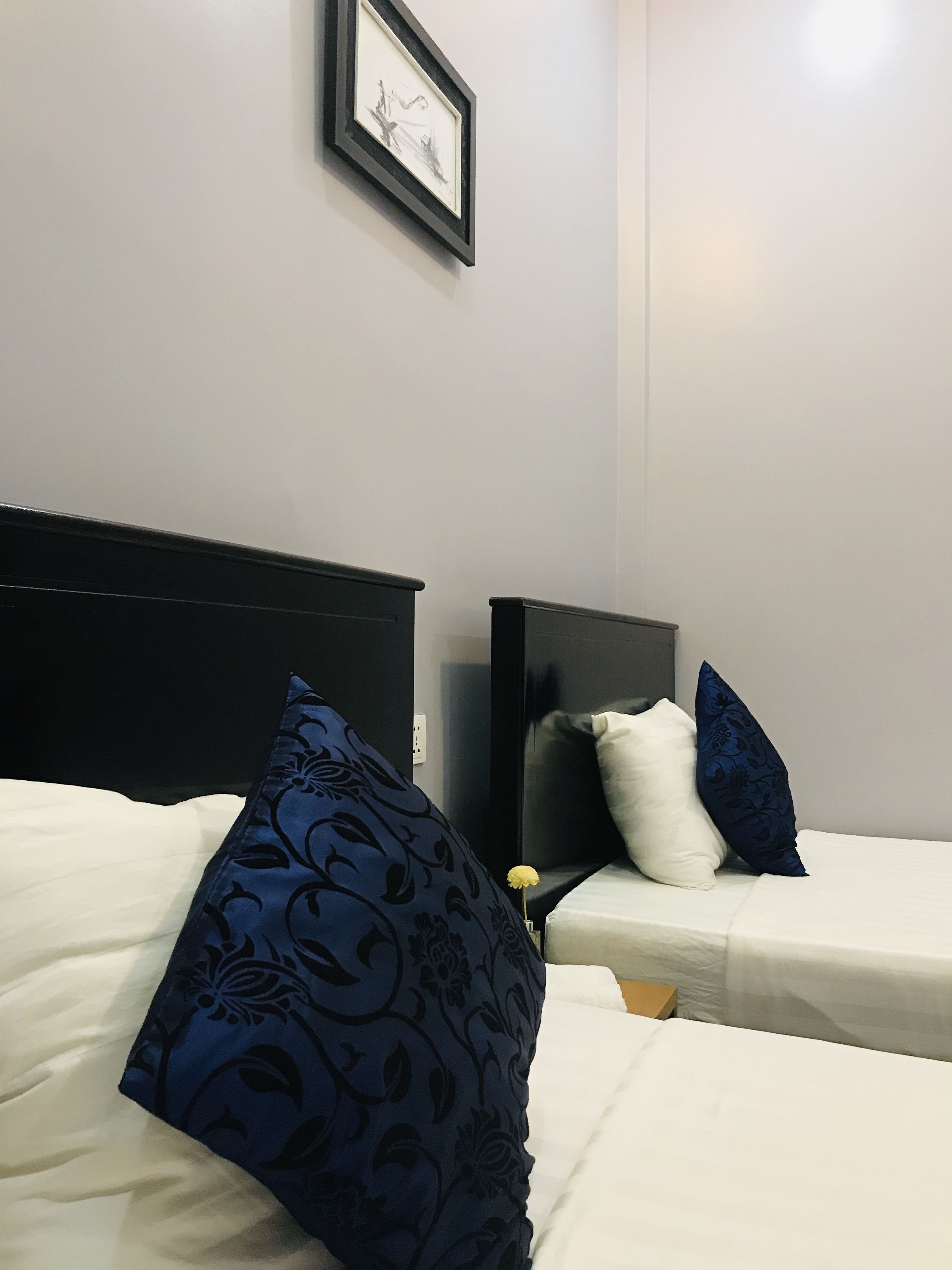 Quarto de hotel com duas camas, cada uma com cabeceira e almofadas. Há um quadro emoldurado na parede acima das camas.