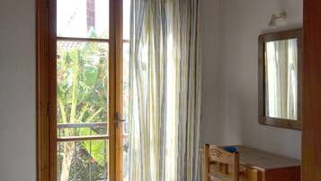 Quarto com porta de madeira, janela com cortinas, beliche, escrivaninha e espelho.